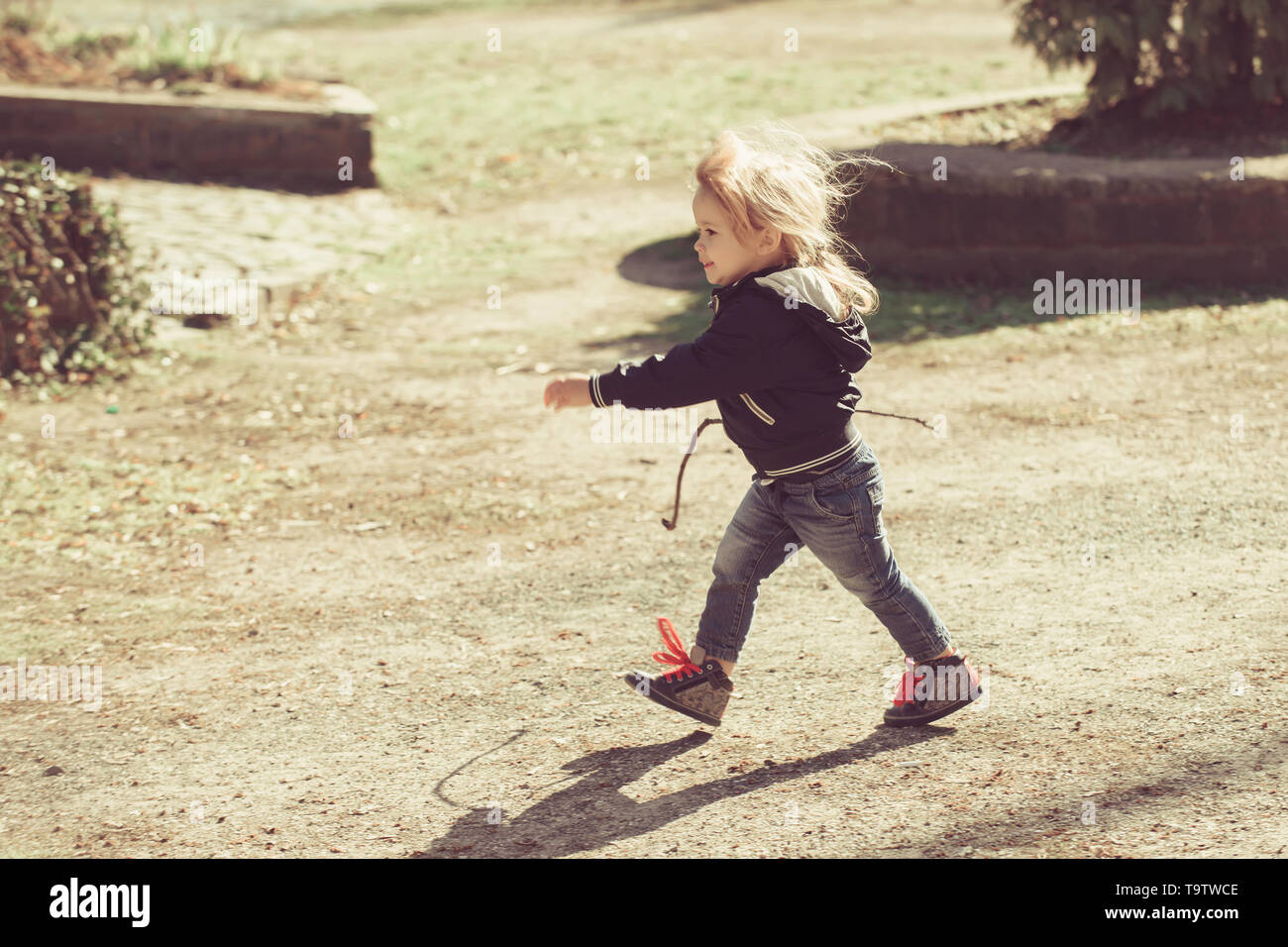 Baby boy in blue jacket and jeans walk with stick Stock Photo - Alamy