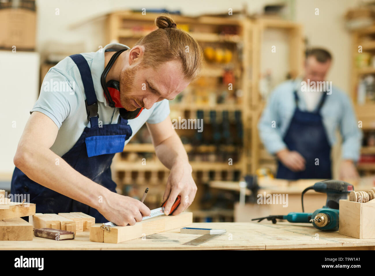 Portrait of contemporary carpenter working with wood standing at tables ...