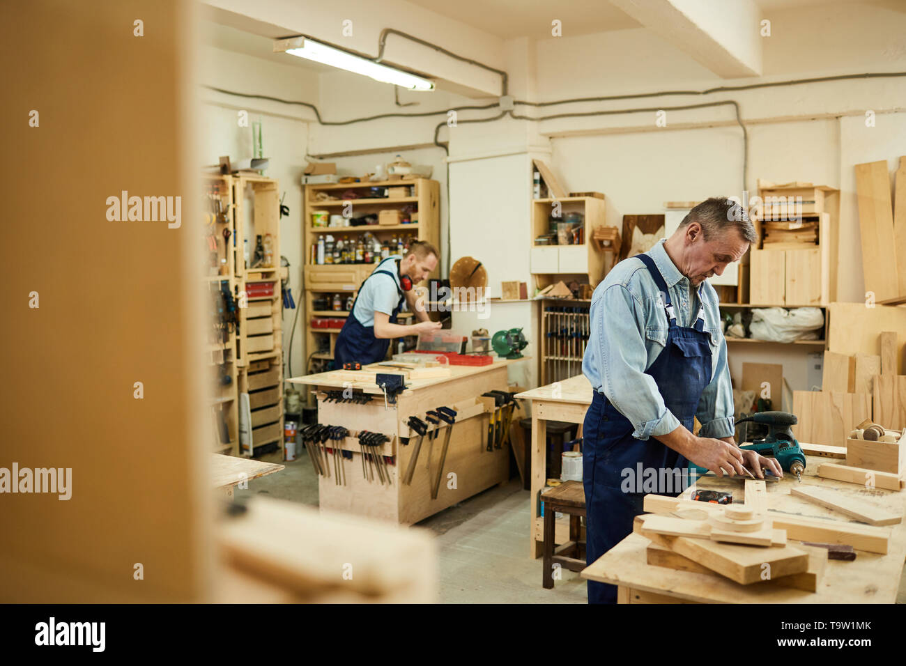 Carpenters Workshop With Two People Assembling Wooden Furniture At