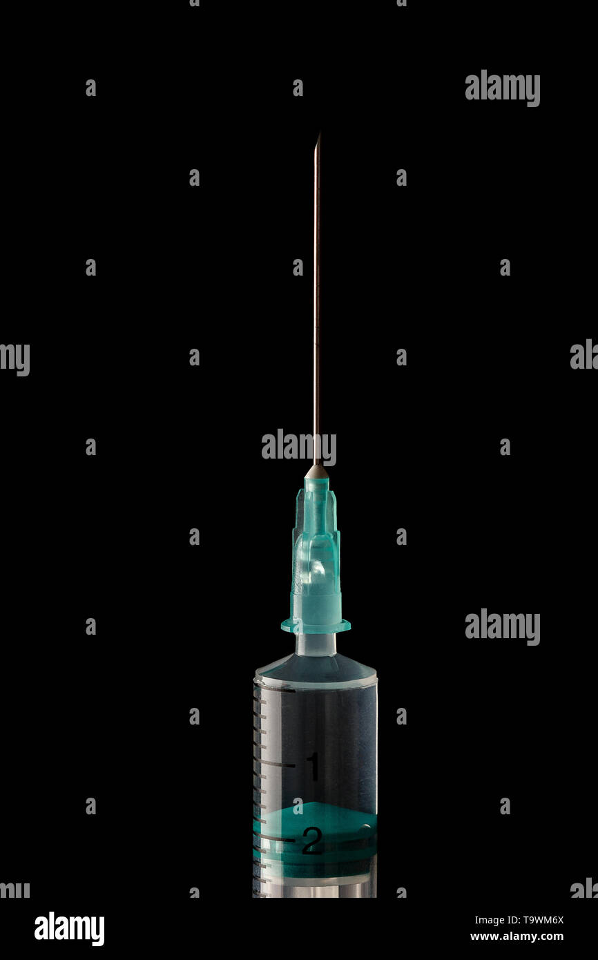 The end of the syringe with a needle filled with liquid on a dark ...