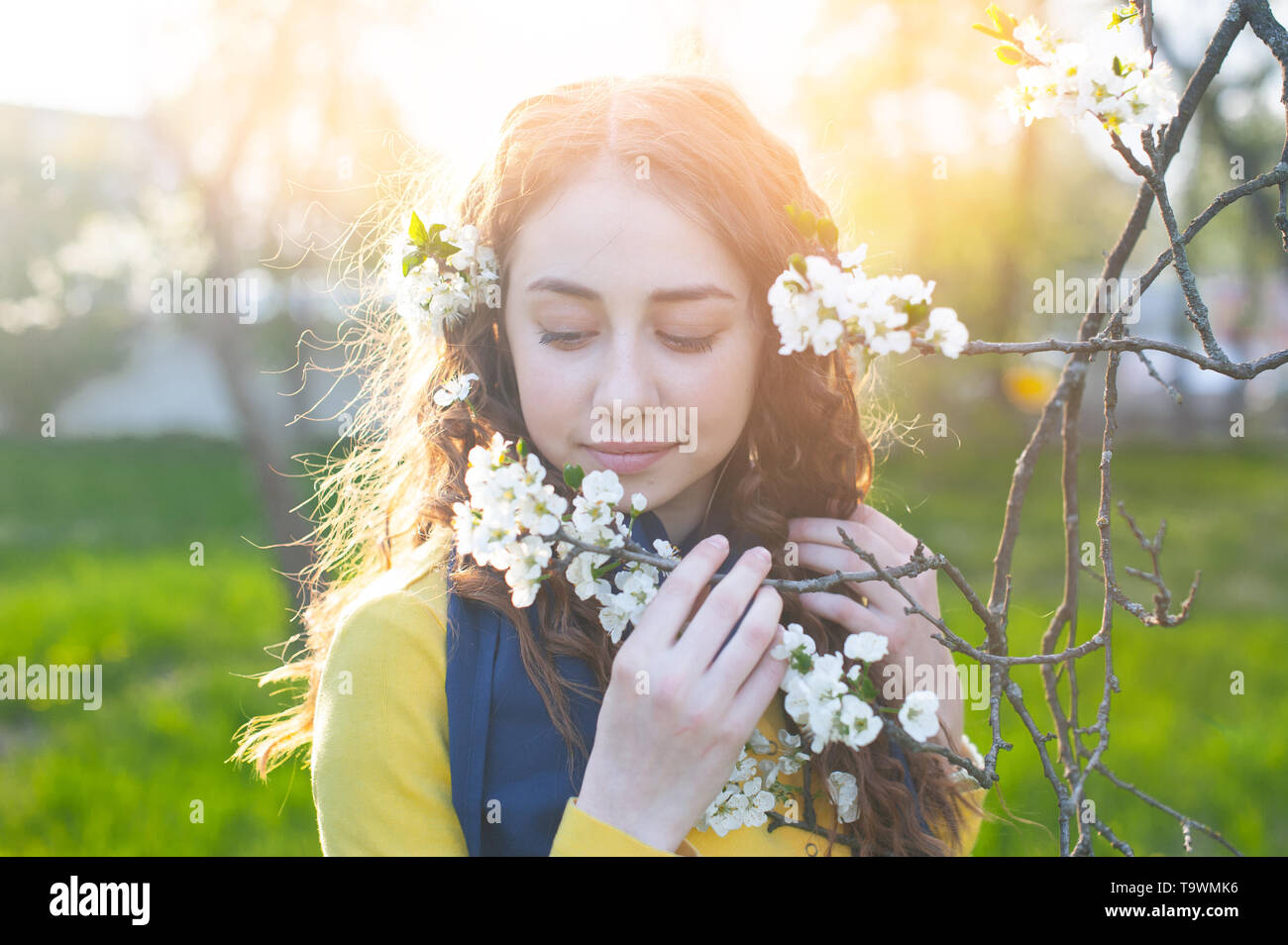 Happy young woman enjoying smell flowers over spring garden background ...