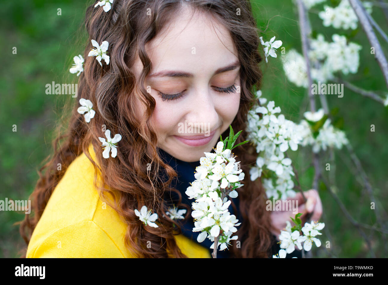 Happy young woman enjoying smell flowers over spring garden background ...