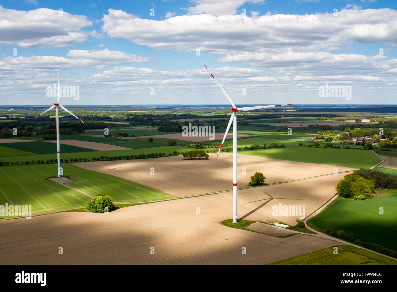 Two wind turbines from eye level with shadows on the ground and clouds ...