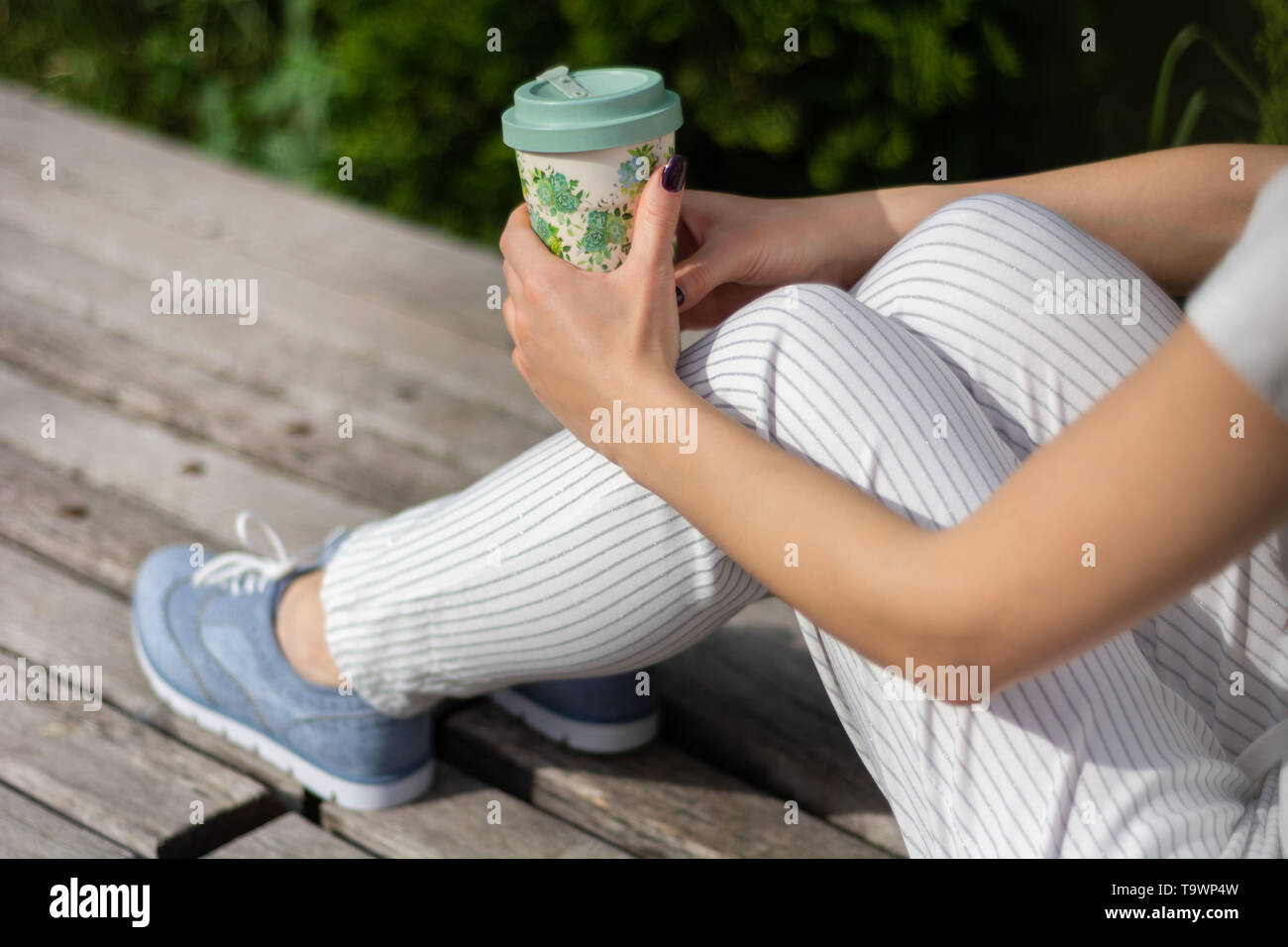 Girl hands holding a cup of coffee on legs in striped pants and sitting ...