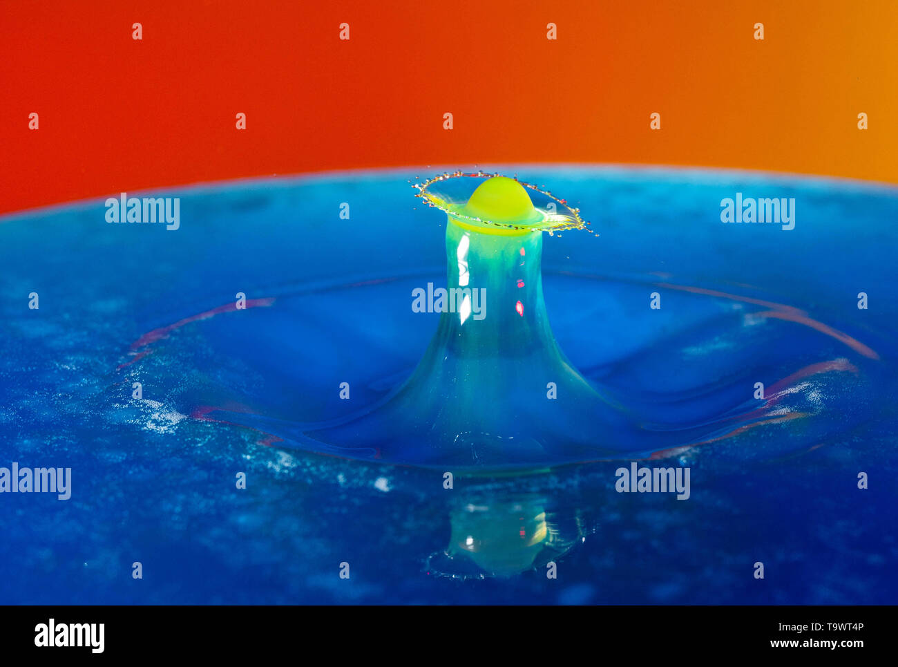 Yellow drop falling into blue water, causing amazing unique ripples ...