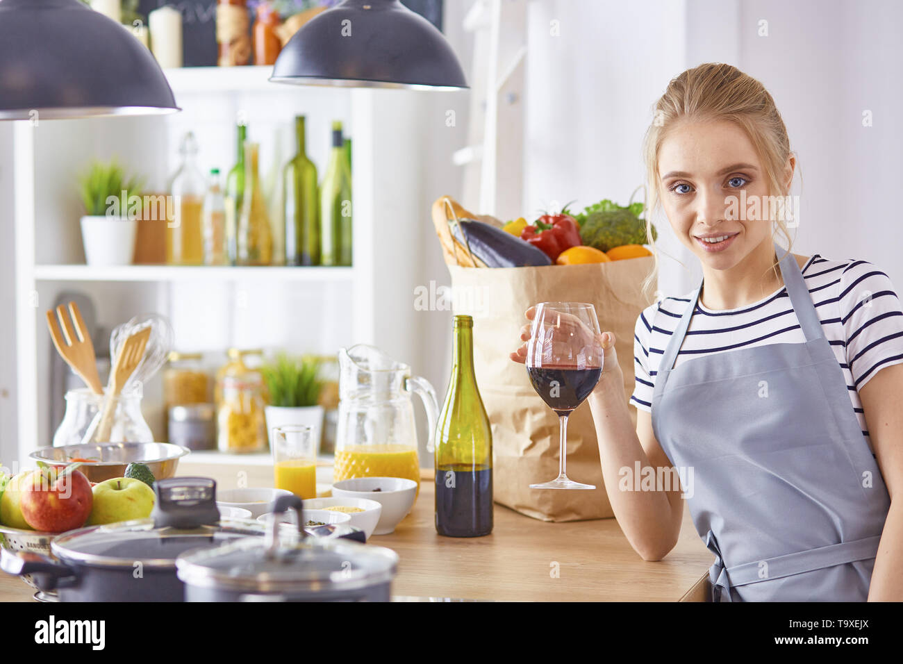 Beautiful woman in kitchen is drinking red wine Stock Photo - Alamy