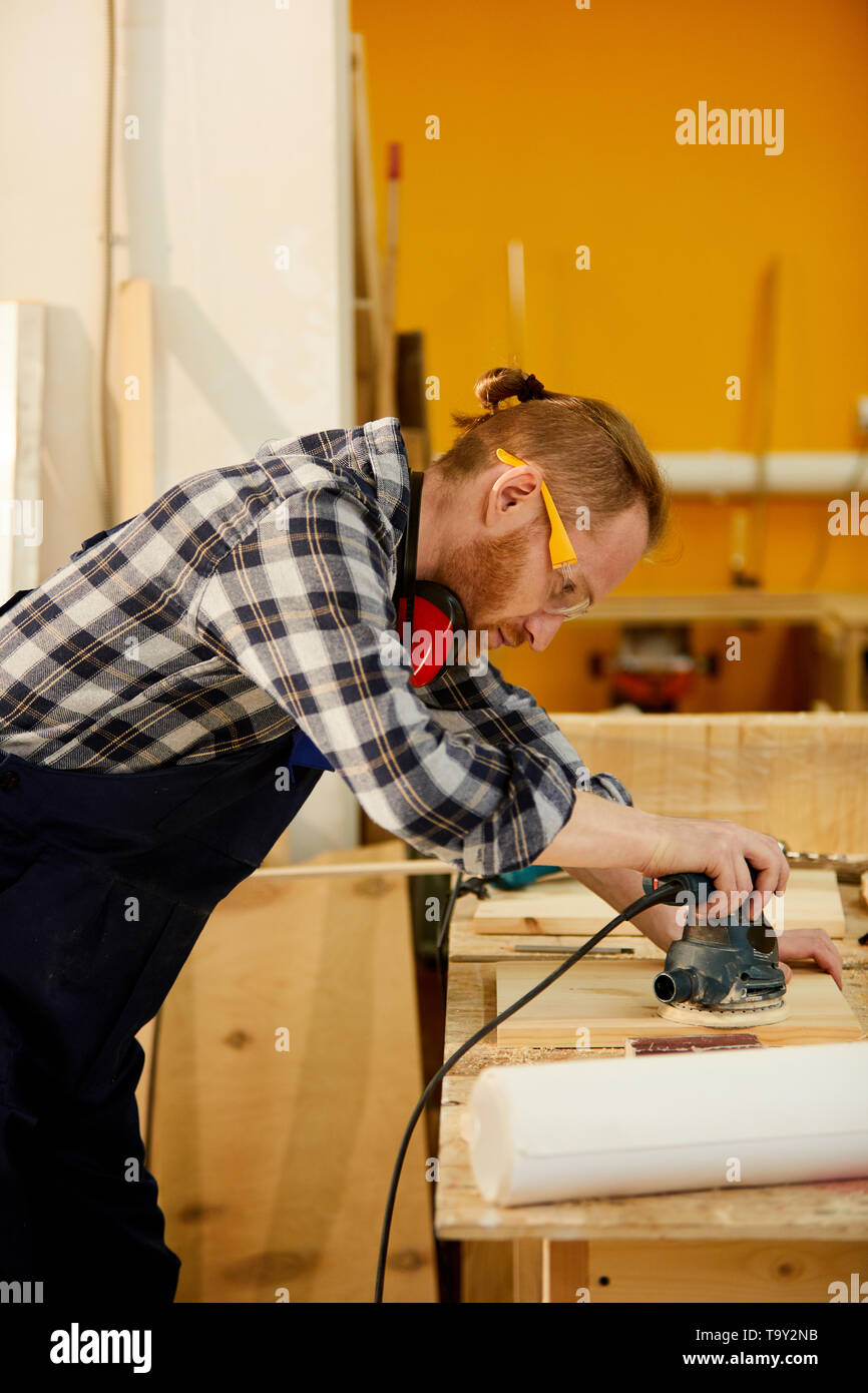 Side view portrait of contemporary carpenter polishing wood while ...