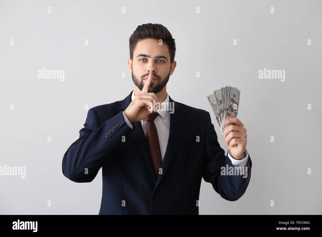 Businessman with bribe showing silence gesture against light background ...