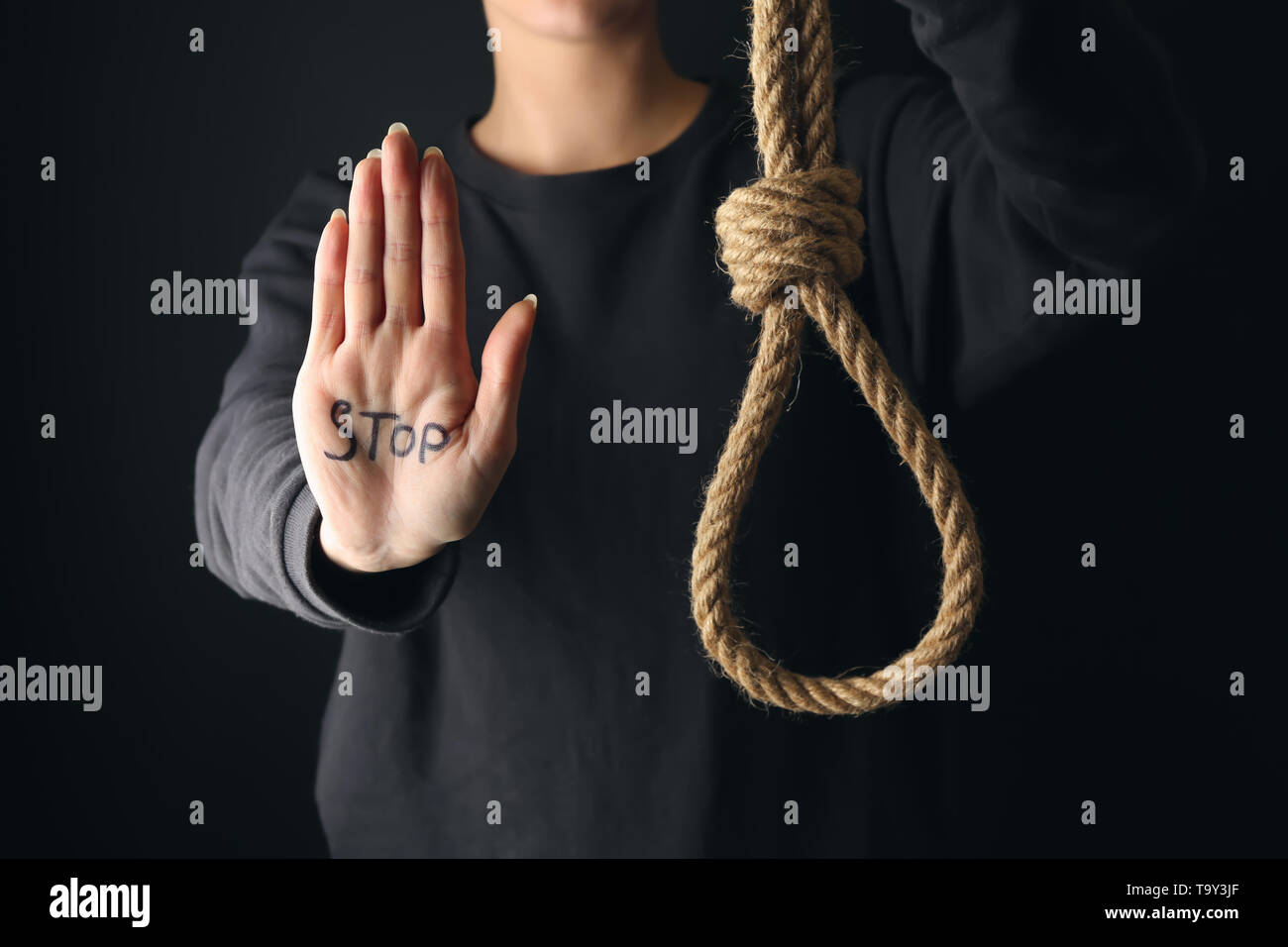 Word STOP written on palm of woman and rope with noose against dark ...