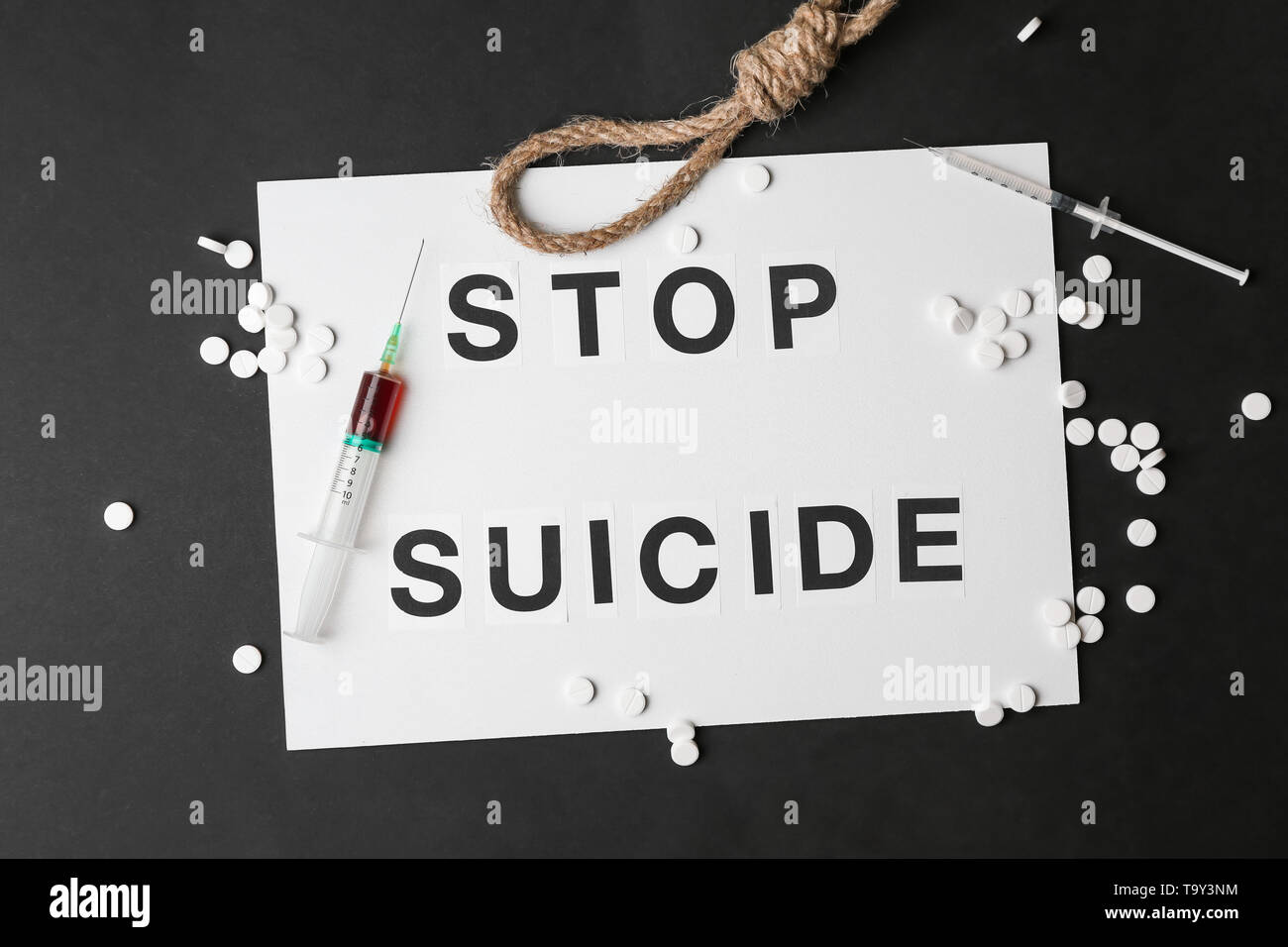 Paper sheet with text STOP SUICIDE, drugs and noose on dark background ...