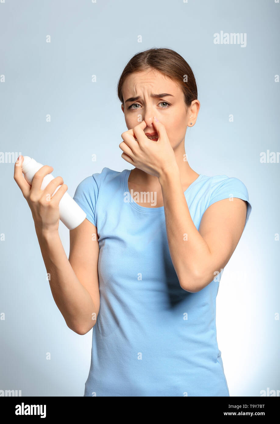 Beautiful young woman with deodorant feeling smell of sweat on light ...
