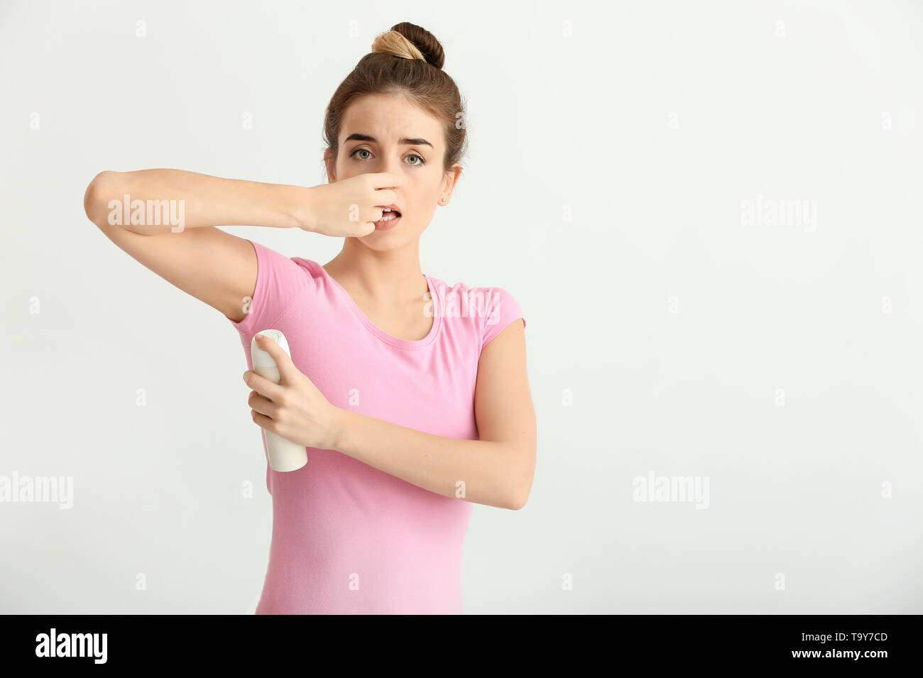 Beautiful young woman with deodorant feeling smell of sweat on light ...