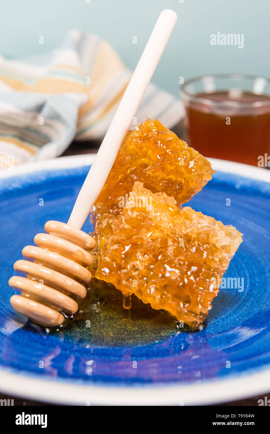 Honey Drops from Pile of Honey Comb and Dipper on blue plate Stock ...