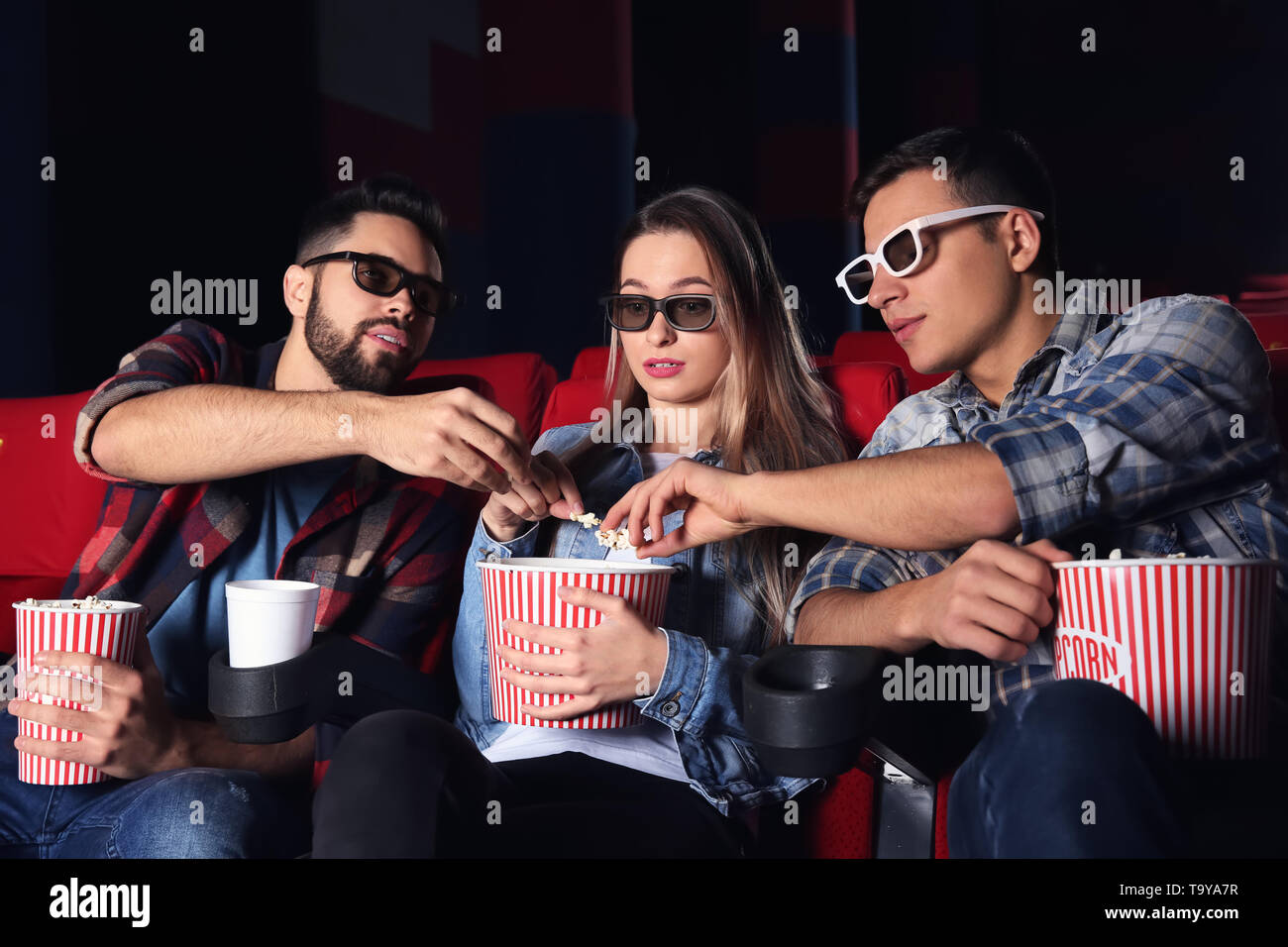 Guys eating popcorn from their friend's bucket in cinema Stock Photo ...
