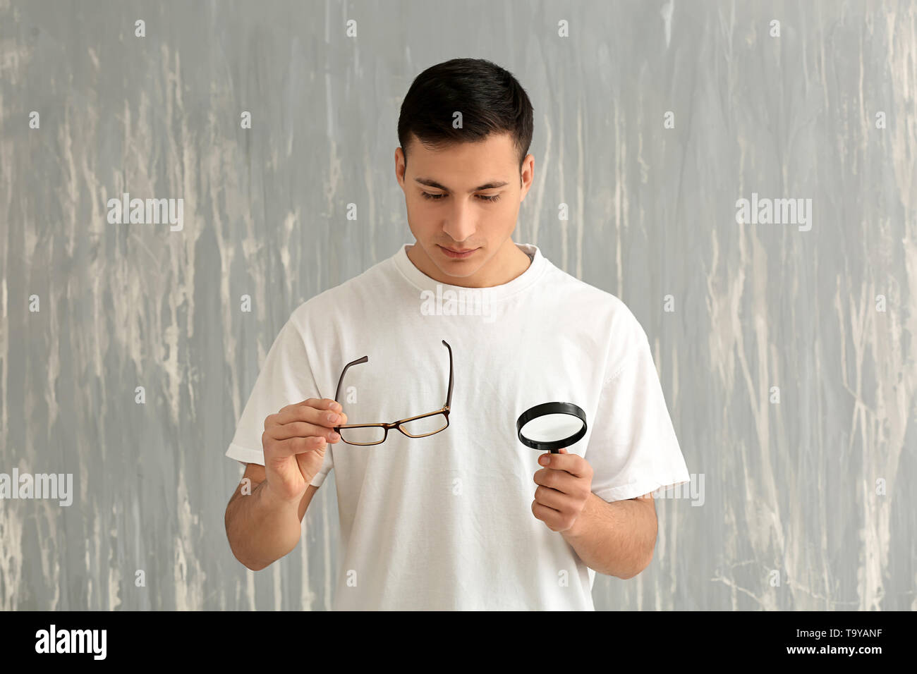 Young man holding eyeglasses and magnifier on grey background Stock ...