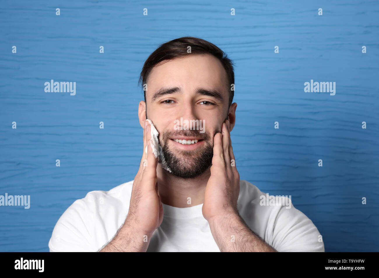 Handsome man applying shaving foam onto his face against color background Stock Photo - Alamy