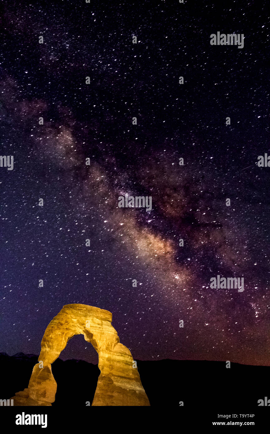 delicate arch at night lit by light with milky way in the background ...