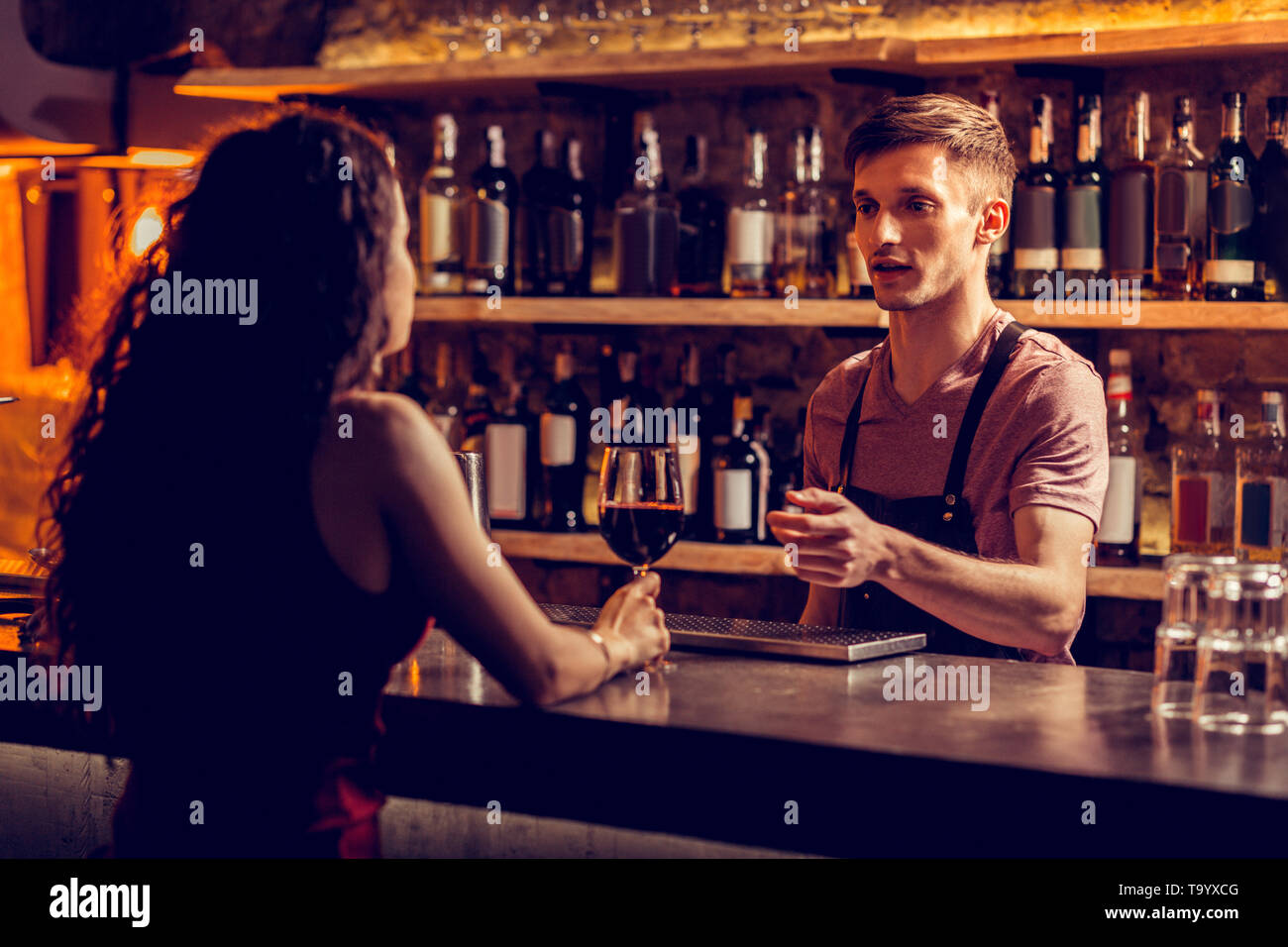 Barman talking to woman sitting at bar counter and drinking Stock Photo ...