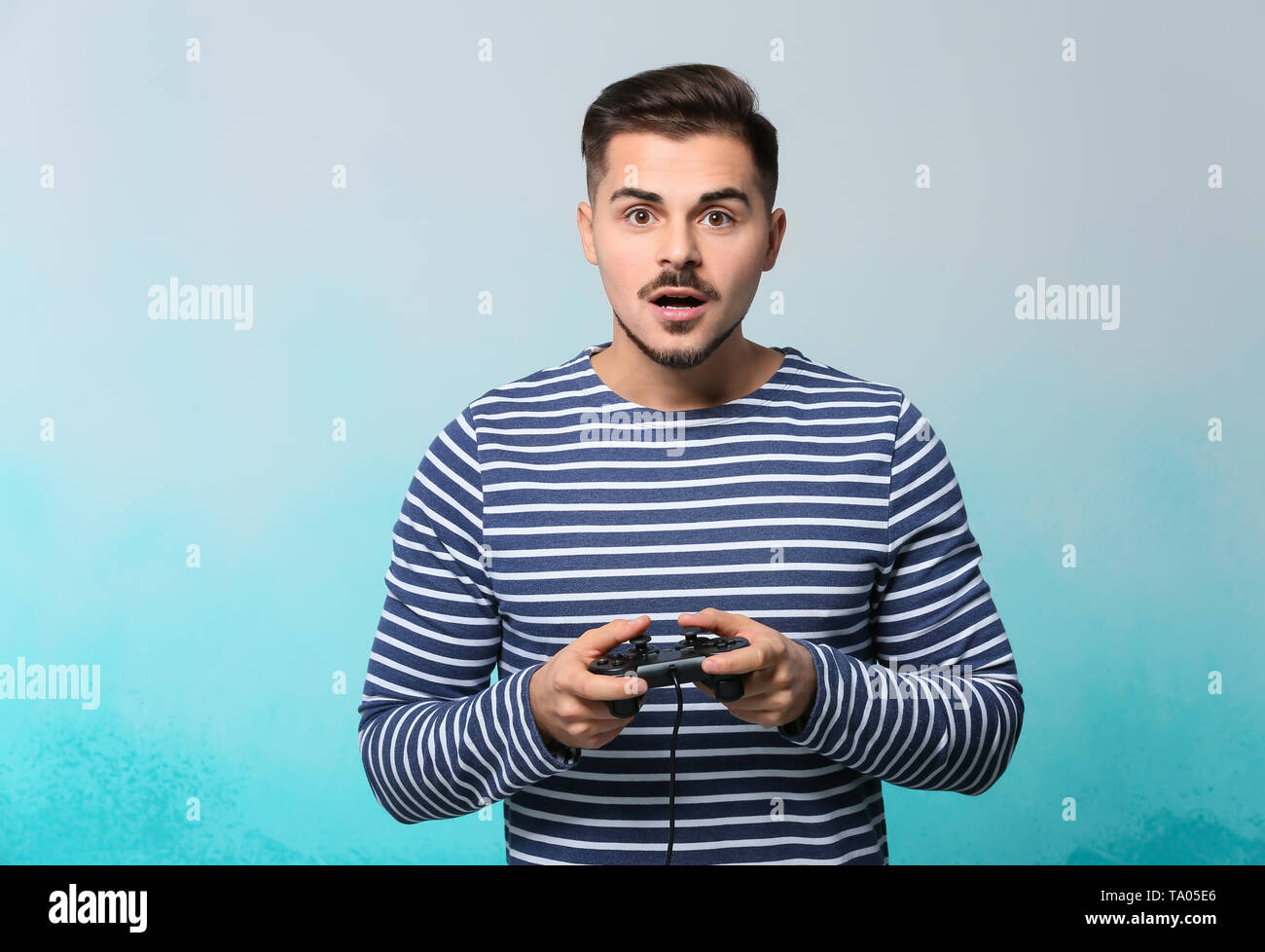 Surprised young man playing video game on color background Stock Photo ...