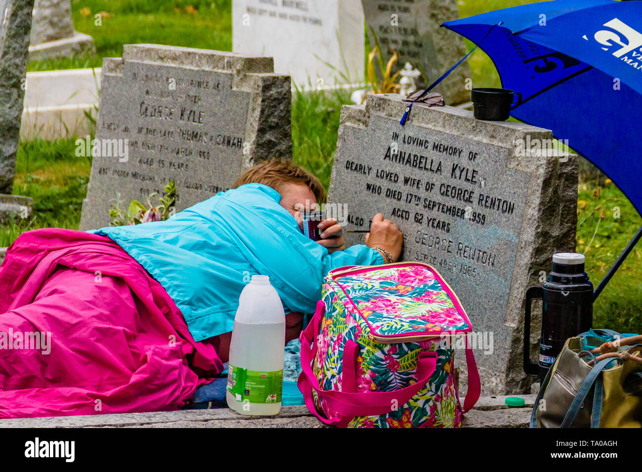 A woman repainting the lettering on a grave headstone in a churchyard ...
