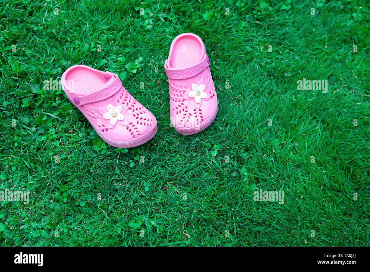 Pink kid's slippers on green lawn. Copy space. Top view, located at ...