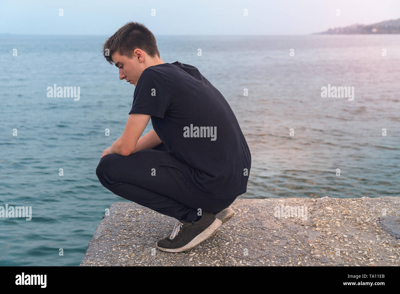 young man crouching on a pier, looking into the sea Stock Photo - Alamy