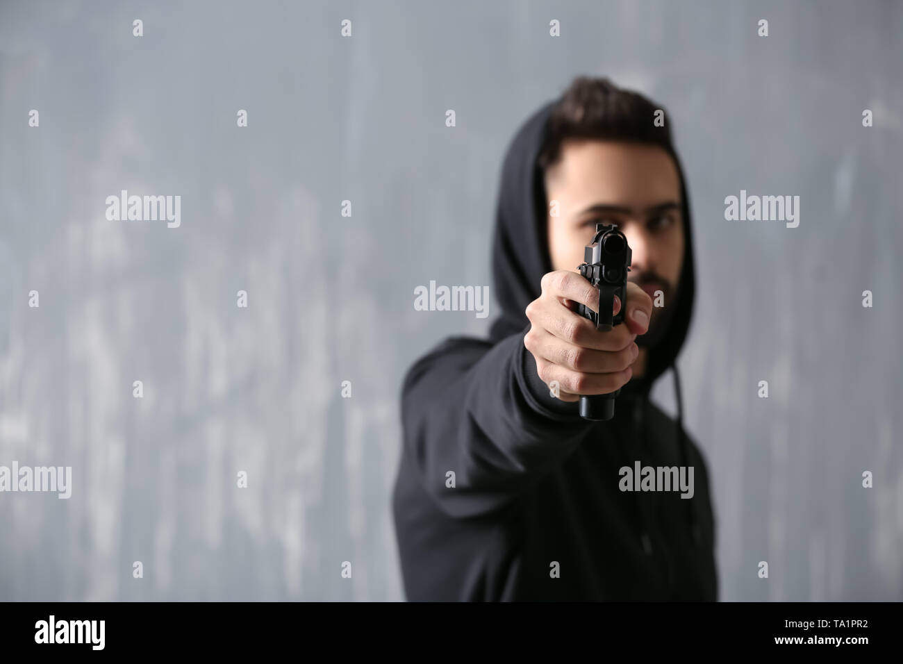 Male criminal pointing a gun at viewer against grey background Stock ...