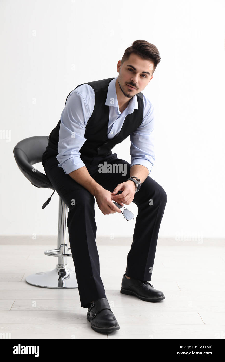 Stylish handsome man sitting on chair near white wall Stock Photo - Alamy