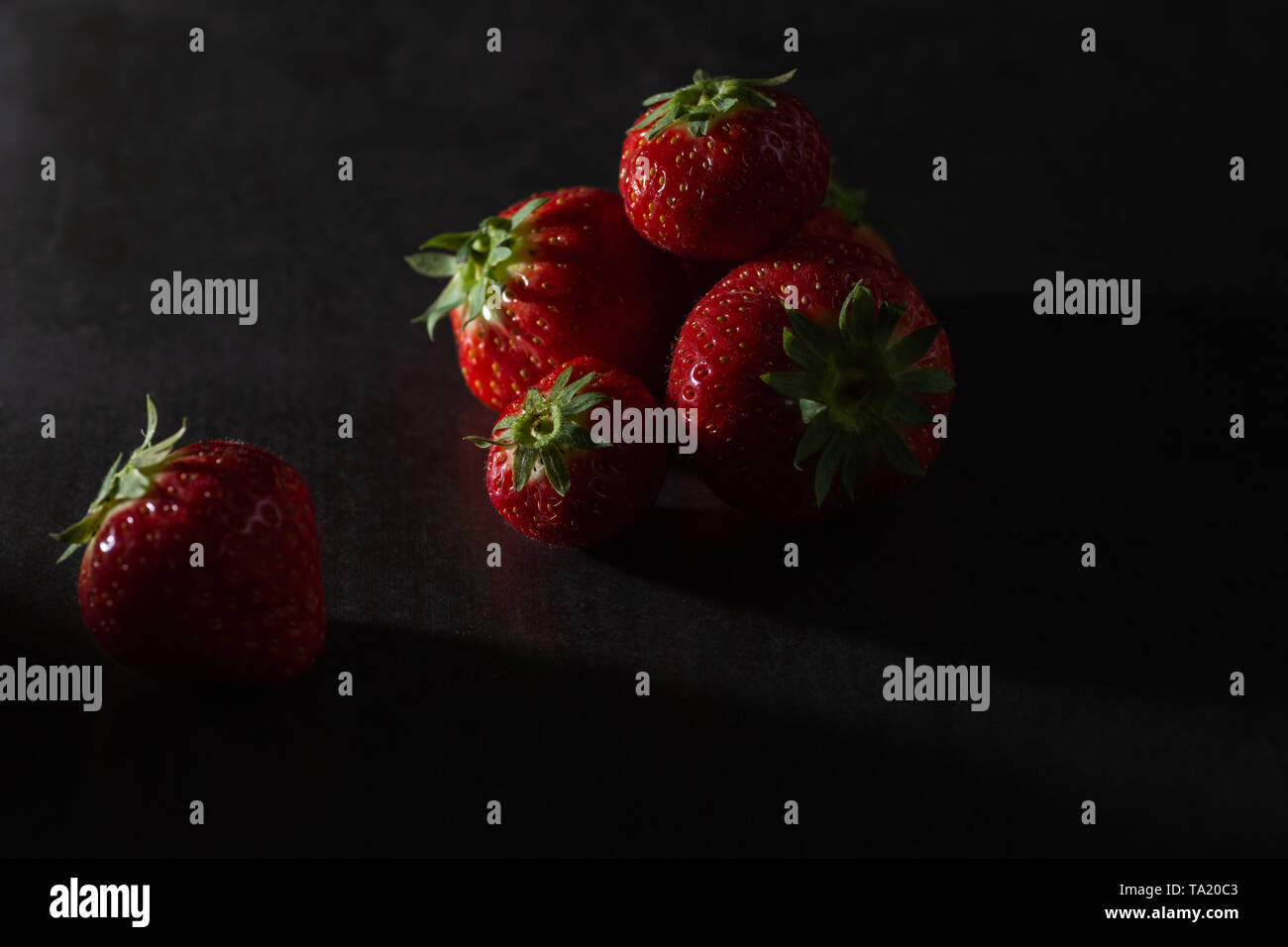 Low key strawberries arranged in a small pile on a dark grey background ...