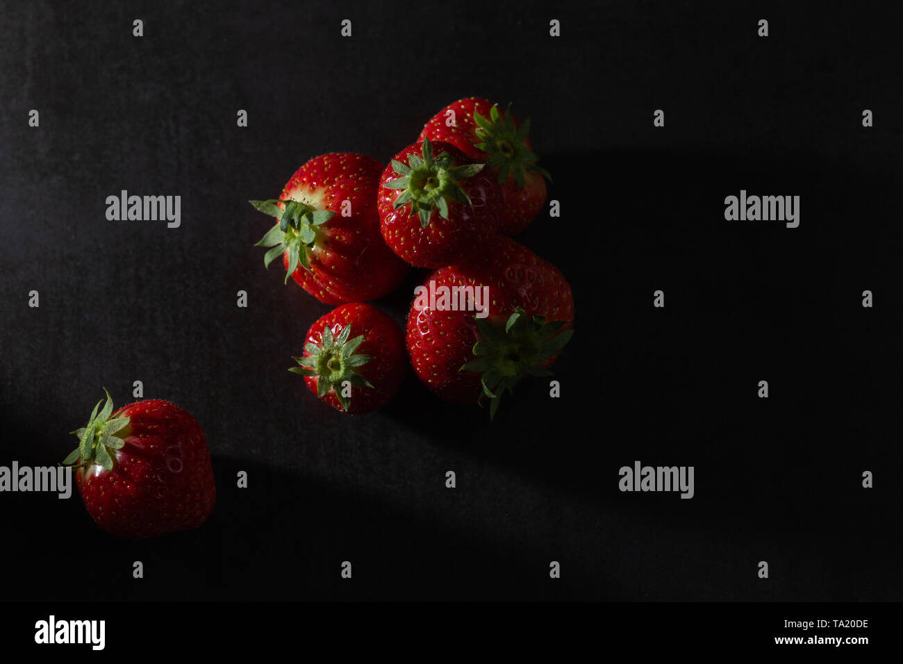 Low key strawberries arranged in a small pile on a dark grey background ...