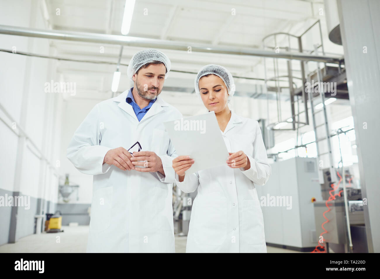 Two technologists in lab coats and masks control the production process ...