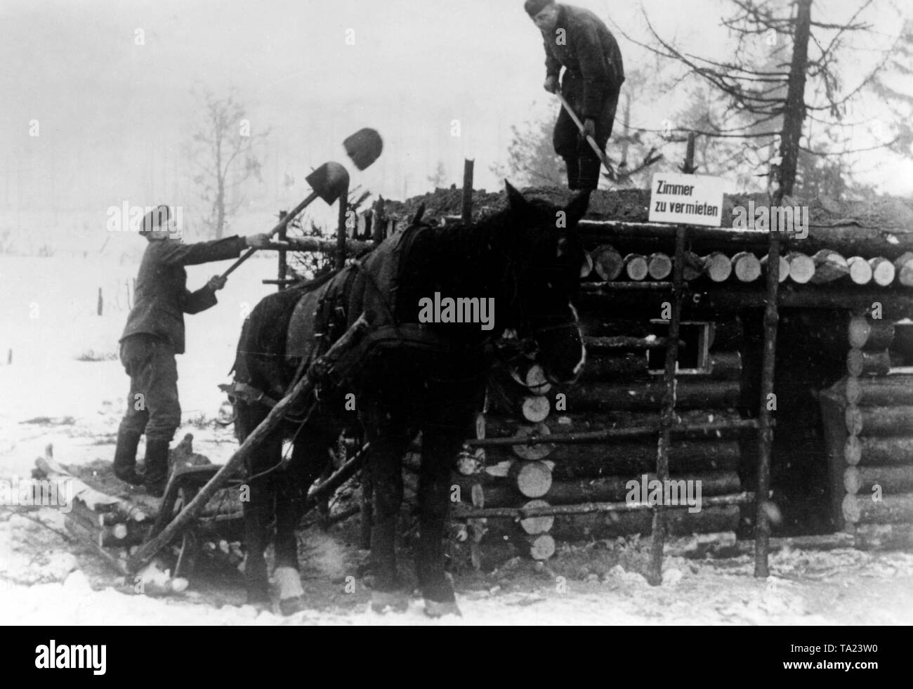 German soldiers build a log cabin southeast of Lake Ilmen. On a sign in ...