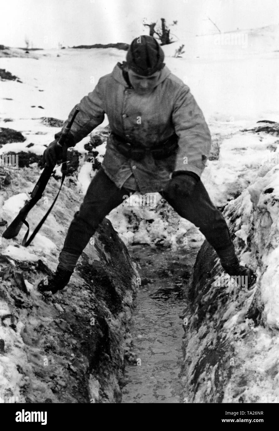 A German soldier balances over a trench full of meltwater. Photo of the ...