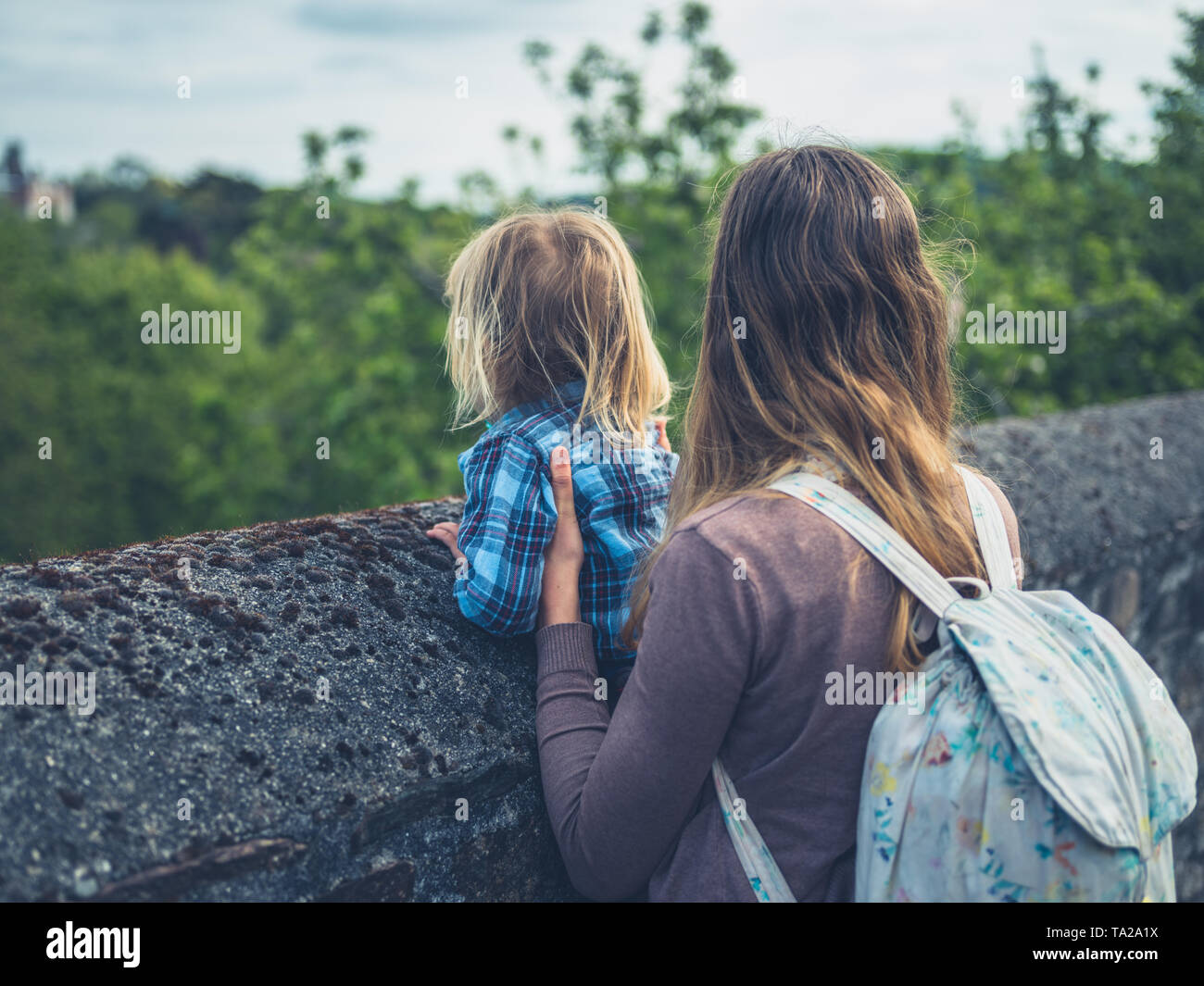 A young mother is lifting up her toddler so he can see over a wall ...