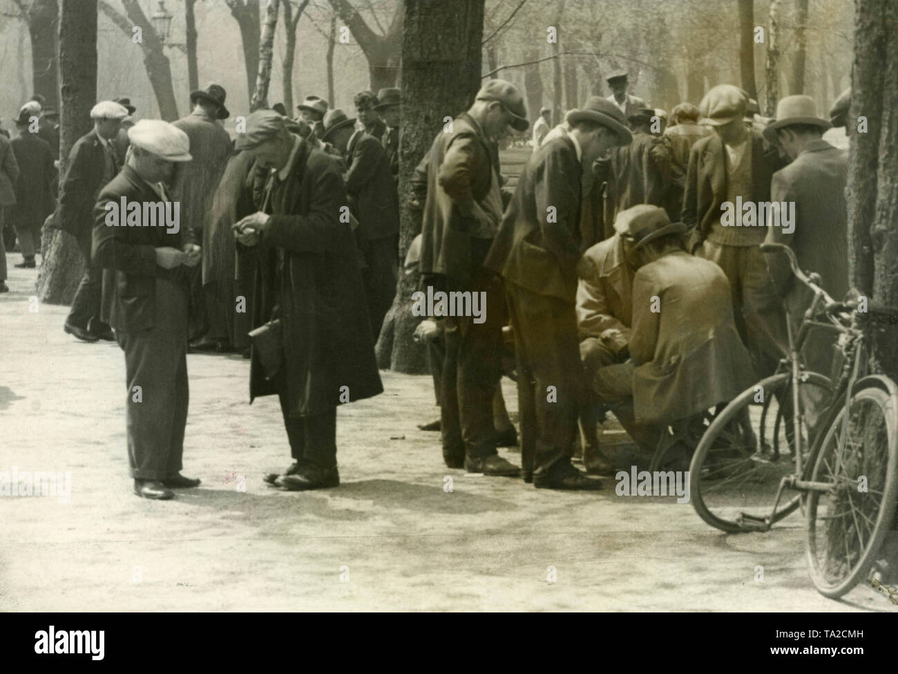 Unemployed men stand in groups in a park in Munich. They probably carry ...