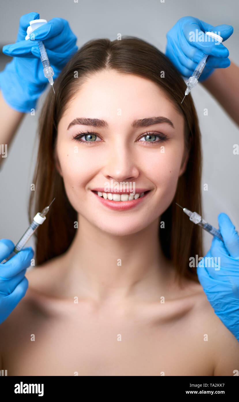 Hands of beauticians holding syringes around pretty doll like woman ...