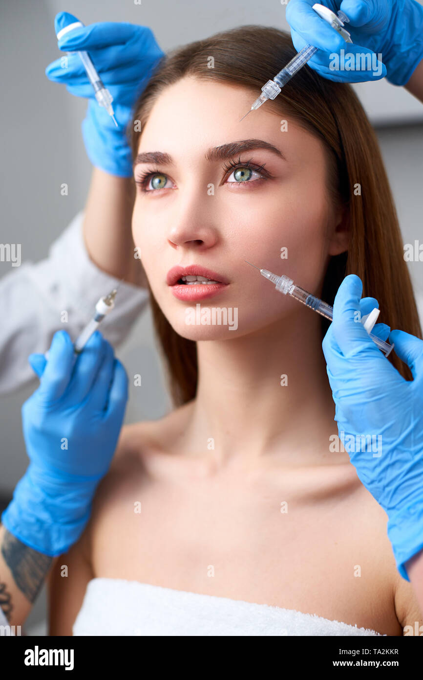 Hands of beauticians holding syringes around doll like woman face ready ...