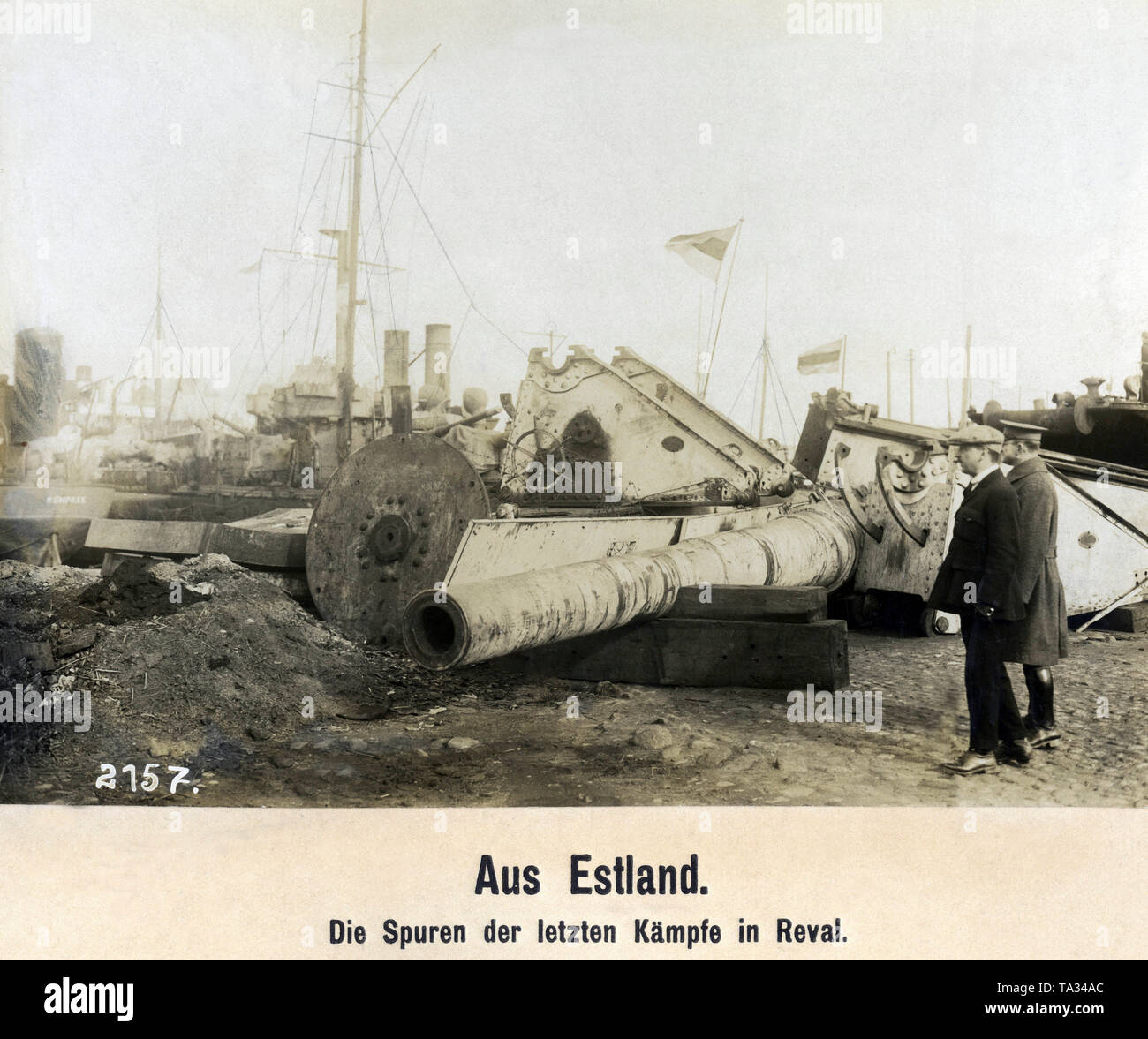 Two men look at a destroyed and tilted gun in the port of Reval ...