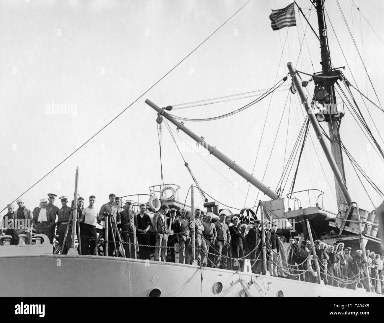 Sailors stand at the stern of an American naval ship and look for ...