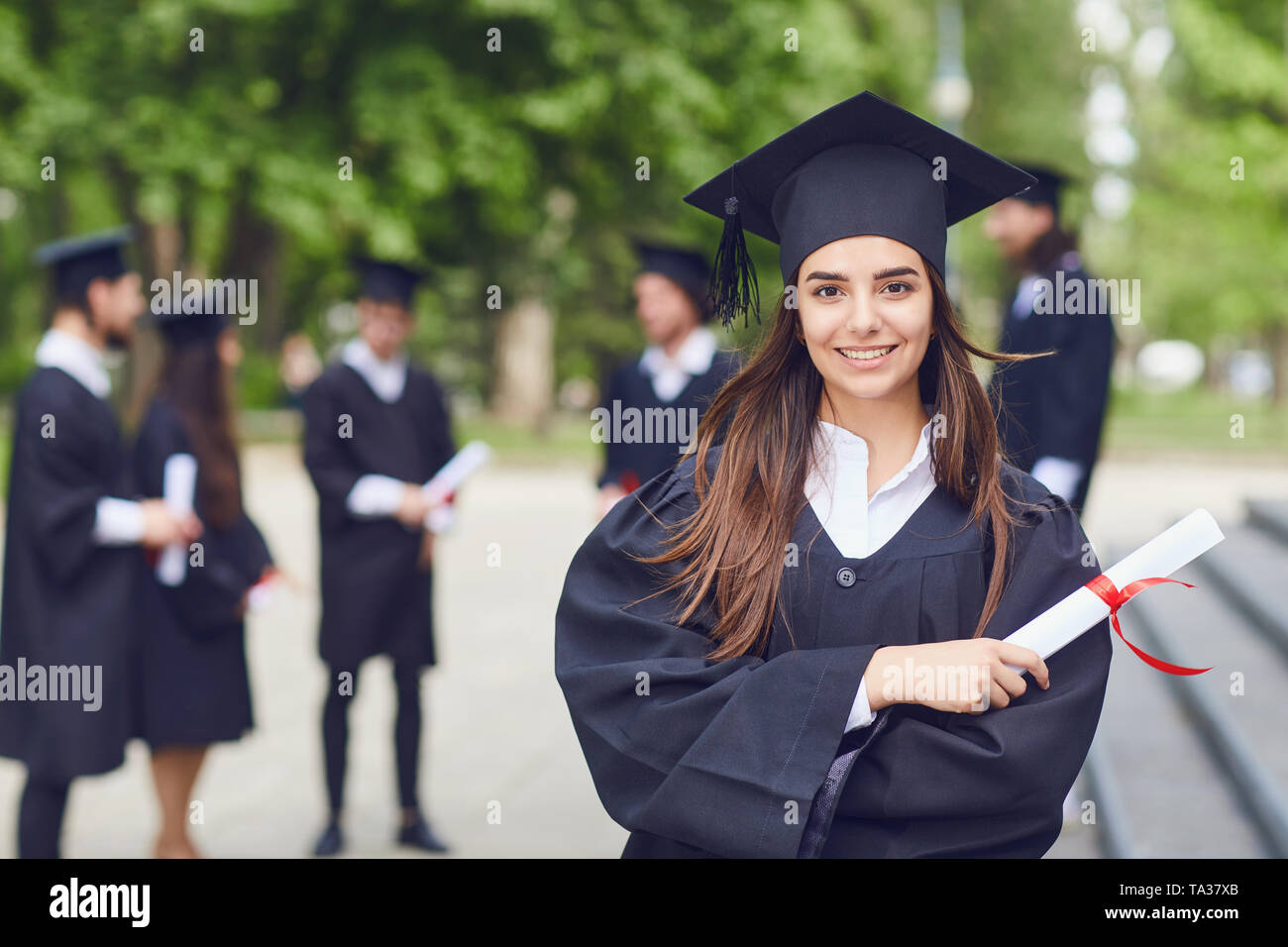 A young female graduate with a scroll in her hands is smiling against ...