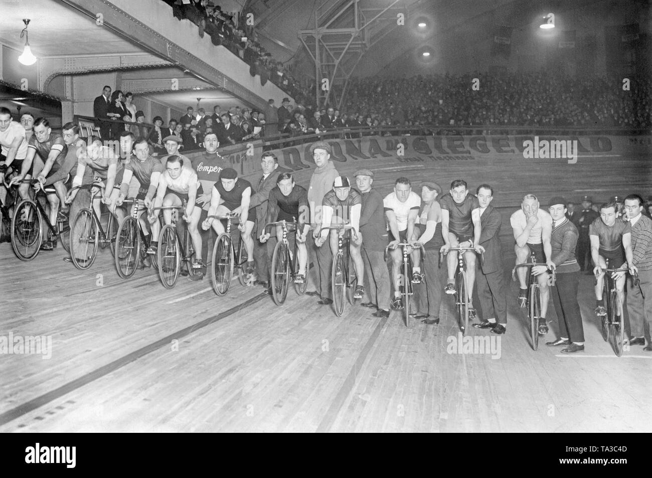 Several racers and their helpers are ready to start a track cycling ...