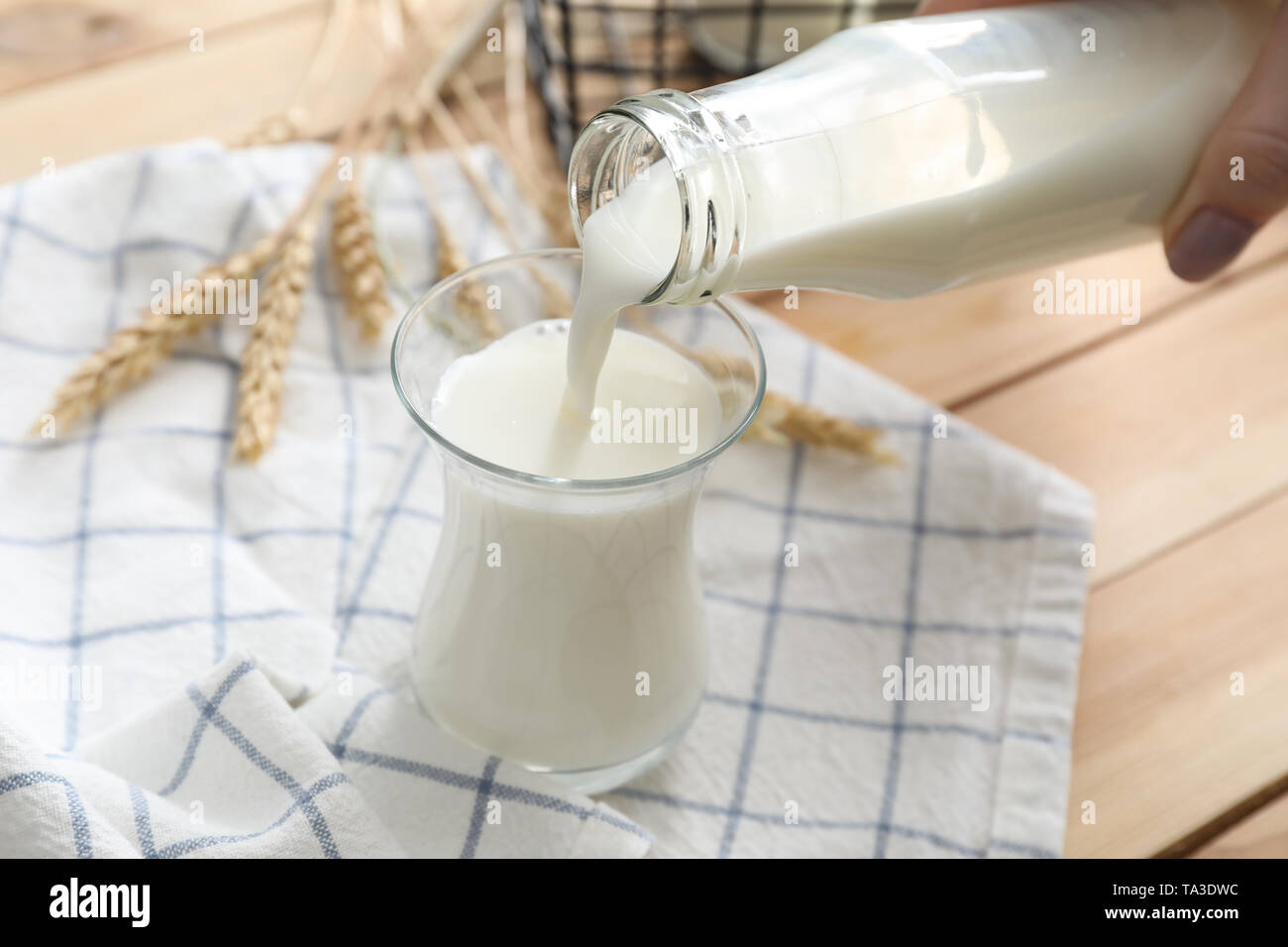 Pouring of fresh milk from bottle into glass on table Stock Photo - Alamy