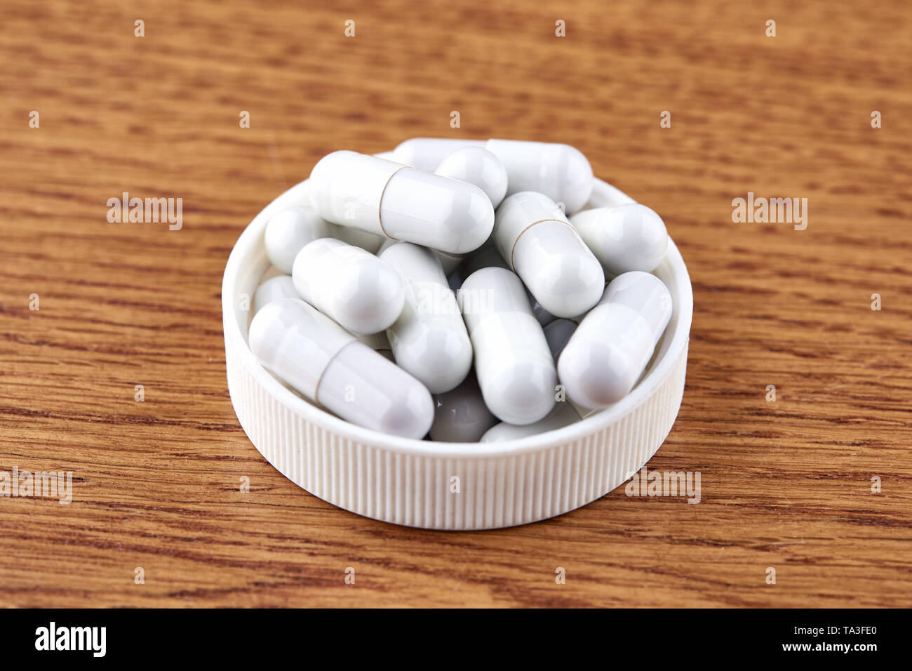 Many white capsules in plastic cap on wooden background Stock Photo - Alamy