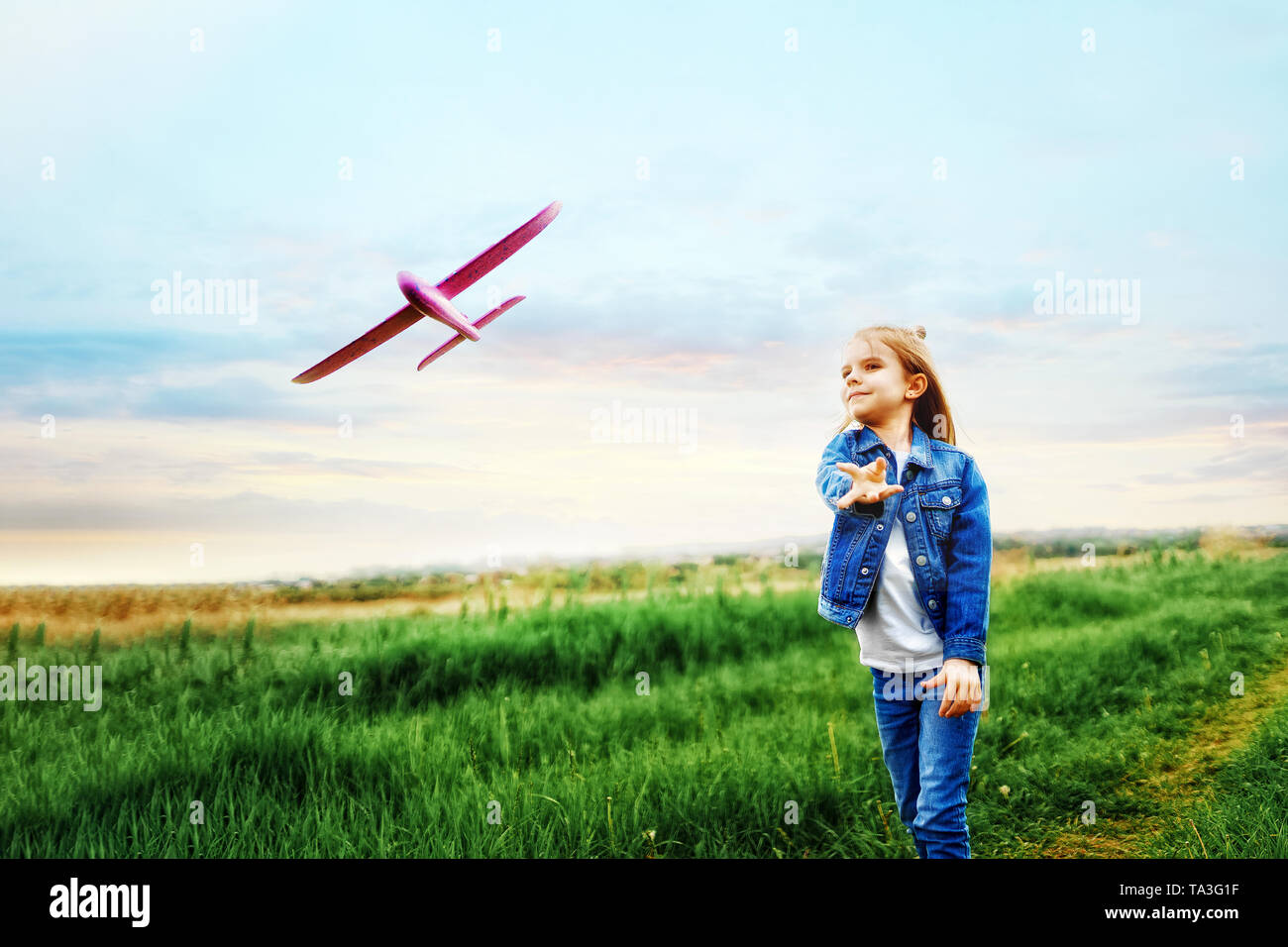 Little girl, launches a toy plane, into the air against, the background ...
