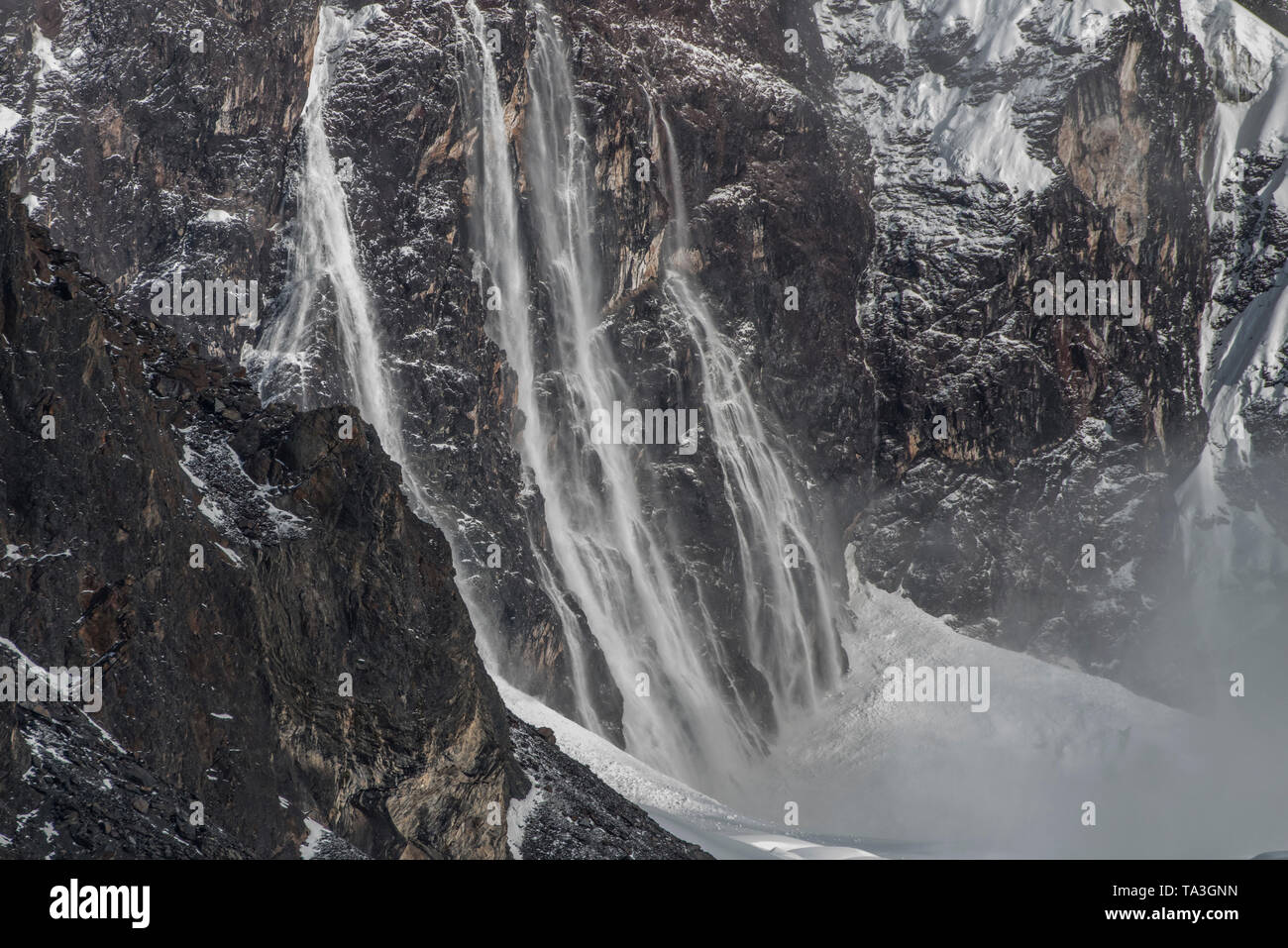 A small avalanche causes snow to fall from a rocky cliff in the Andes ...