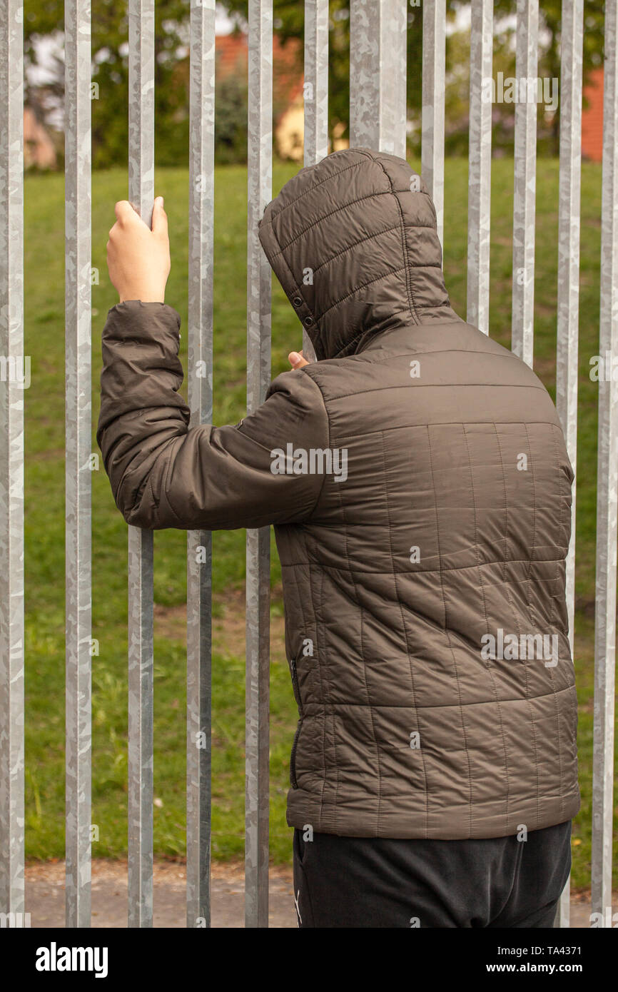Lonely teenager standing outside a metal fence with iron bars and ...