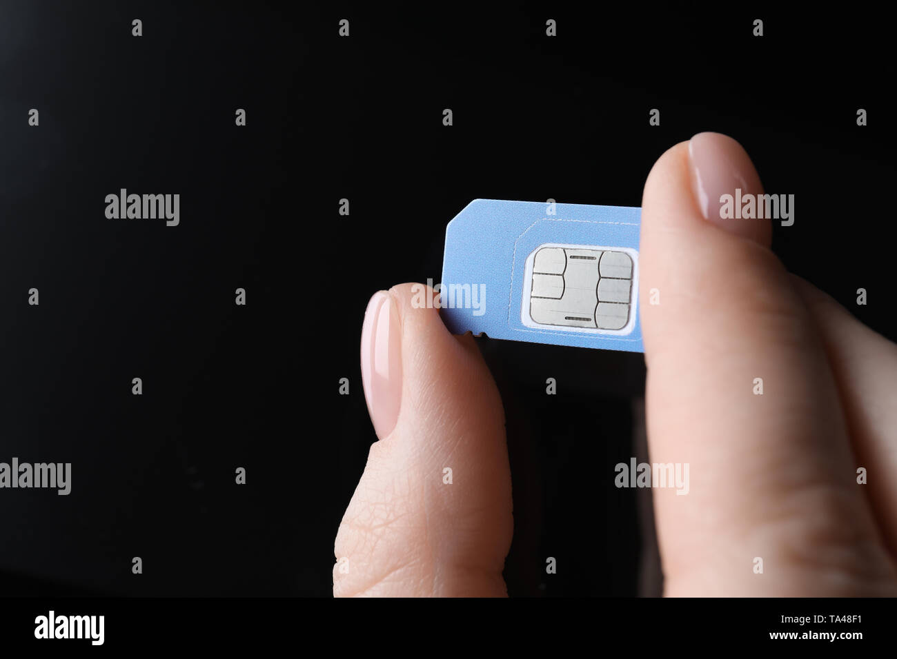 Female hand holding sim card on dark background Stock Photo - Alamy