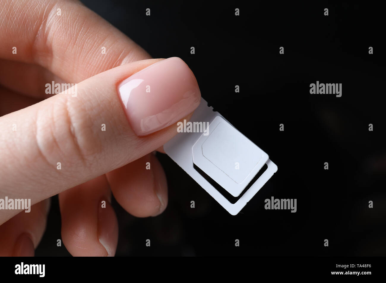 Female hand holding sim card on dark background Stock Photo - Alamy