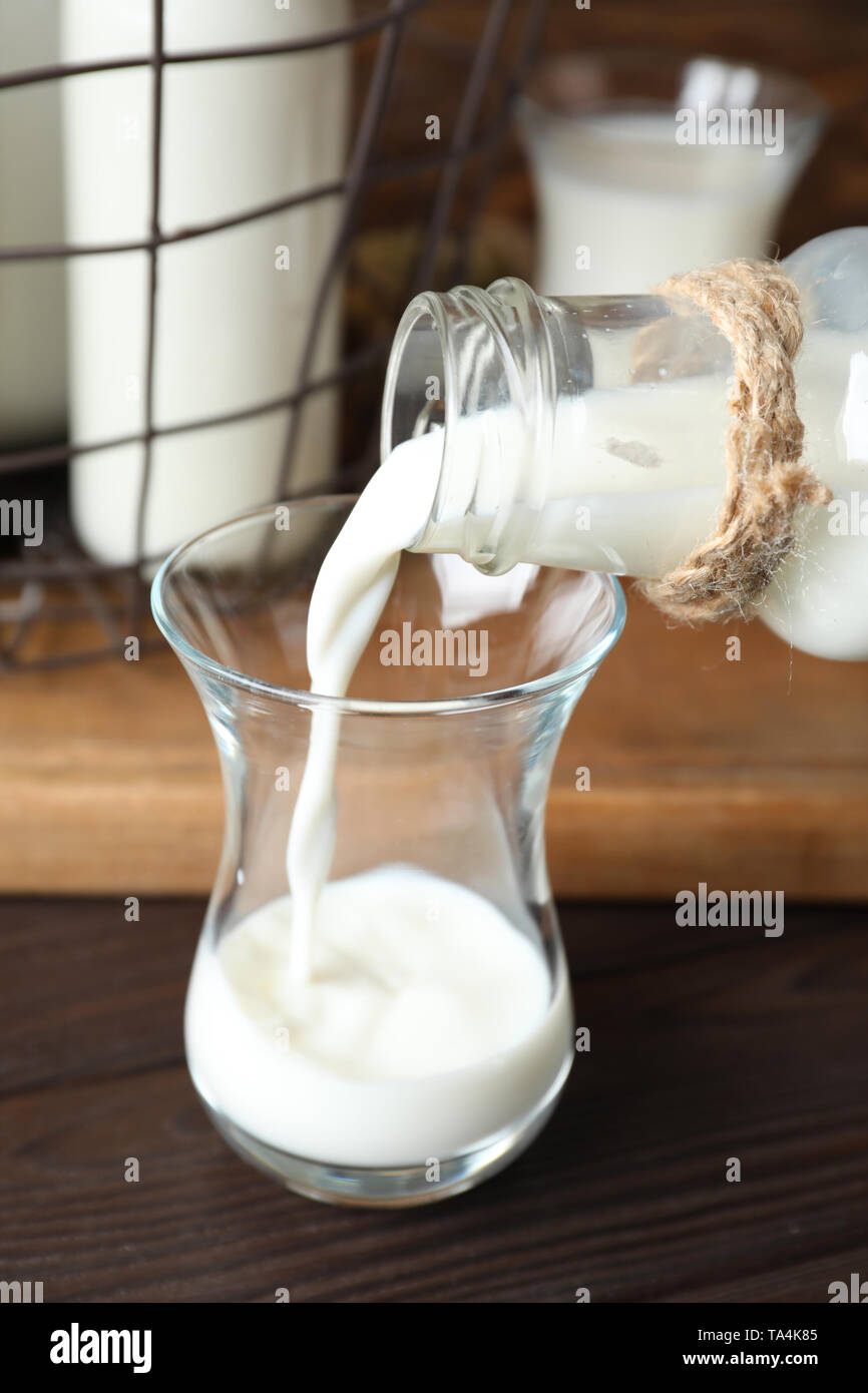 Pouring of fresh milk from bottle into glass on wooden table Stock ...