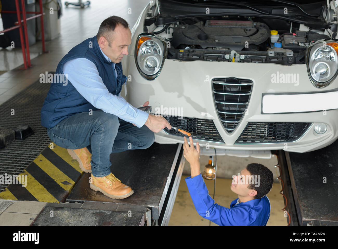 mechanic passing tool to colleague in pit under car Stock Photo - Alamy